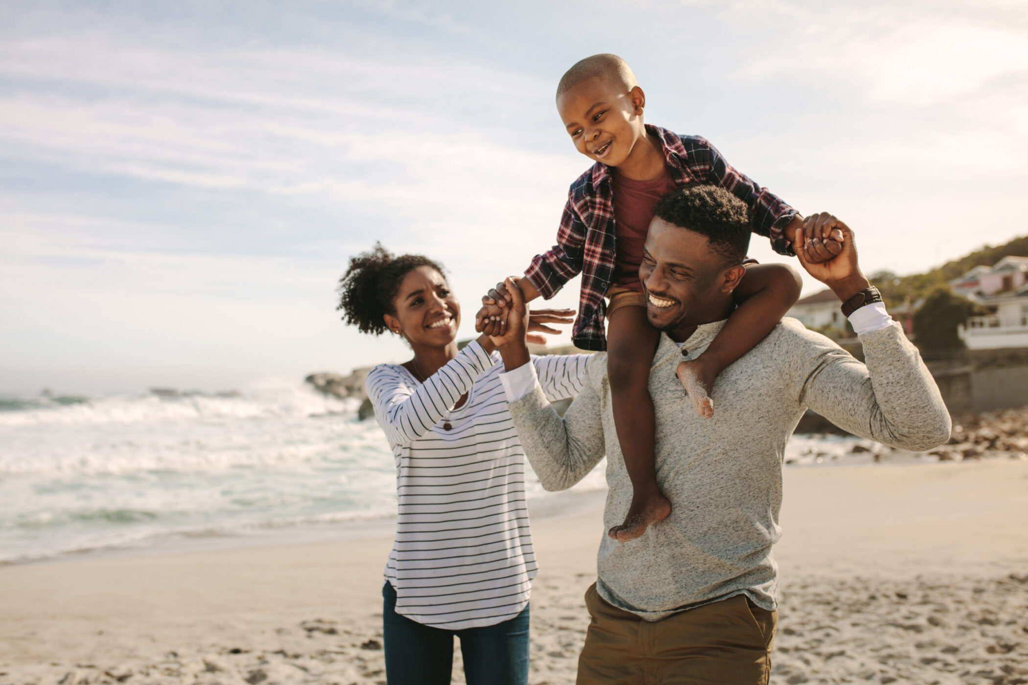 Parents carrying son on shoulders on beach vacation - Globetrender